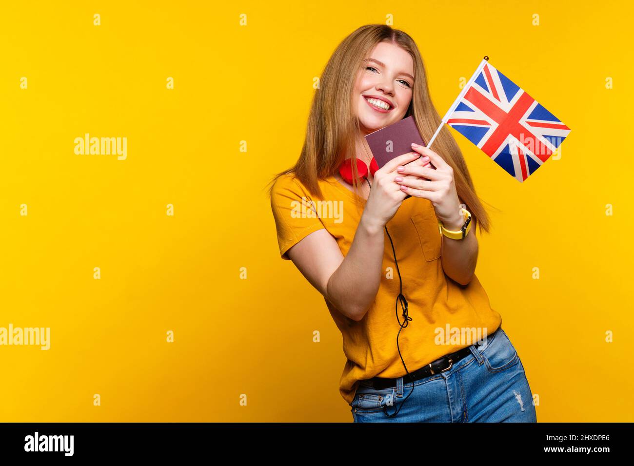 Happy Student girl holds small UK flag and passport in studio on yellow ...
