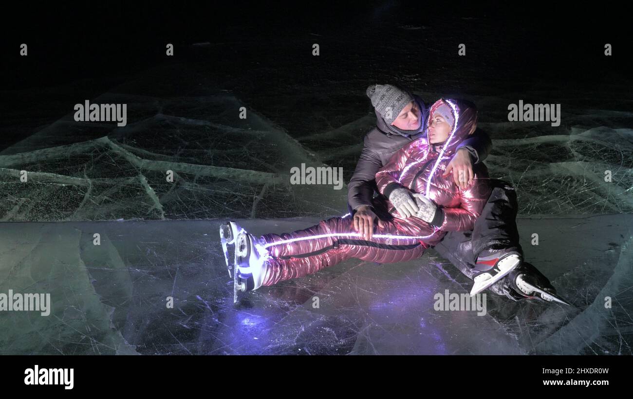 Young loving couple skating at ice rink at night. Man and woman kiss ...