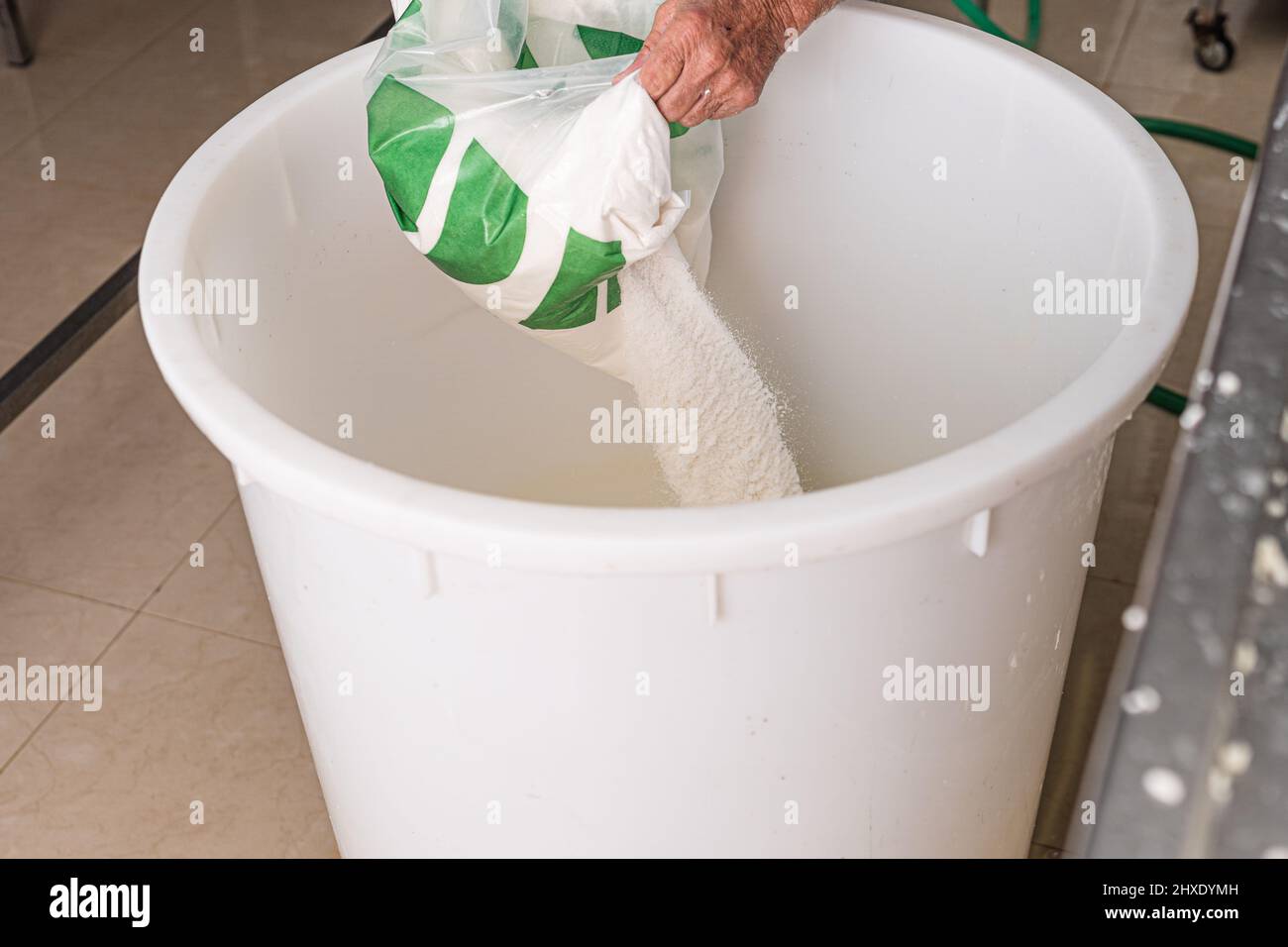 older man's hands pouring salt into plastic container to prepare brine ...