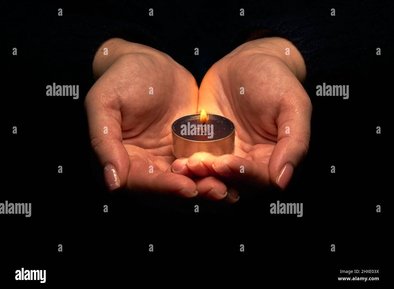 Close-up of hands holding a burning candle in the dark. Adult woman ...