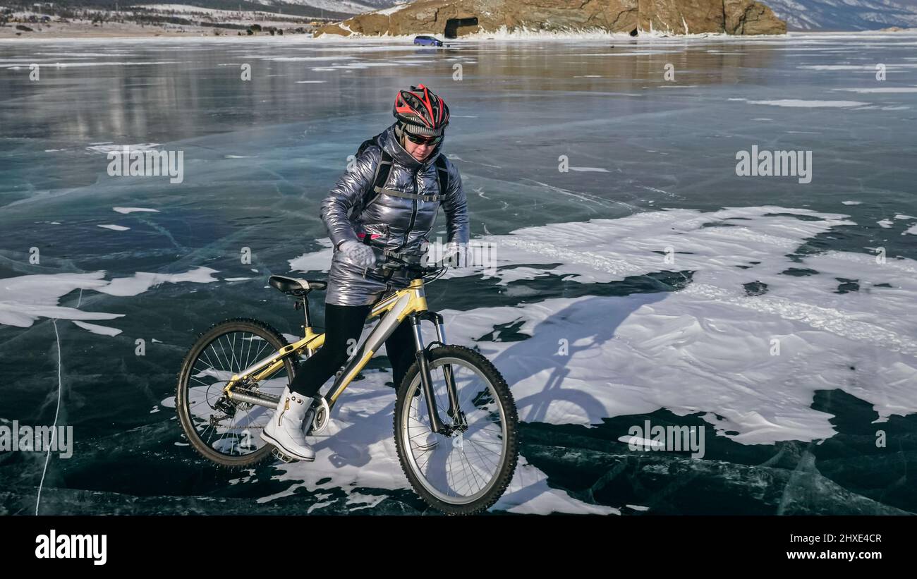 Woman stands near her bike on ice. The girl cyclist stopped to rest ...