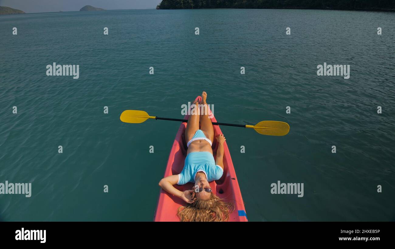 Pretty slim woman in elegant swimsuit lies in pink plastic kayak ...