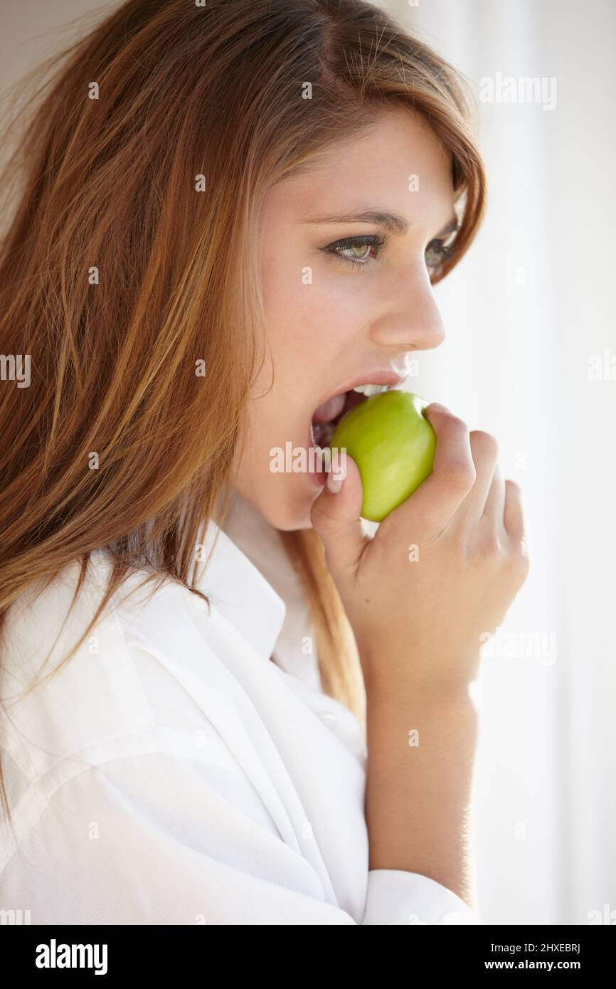 Biting into a juicy green apple. A beautiful young woman biting into a ...