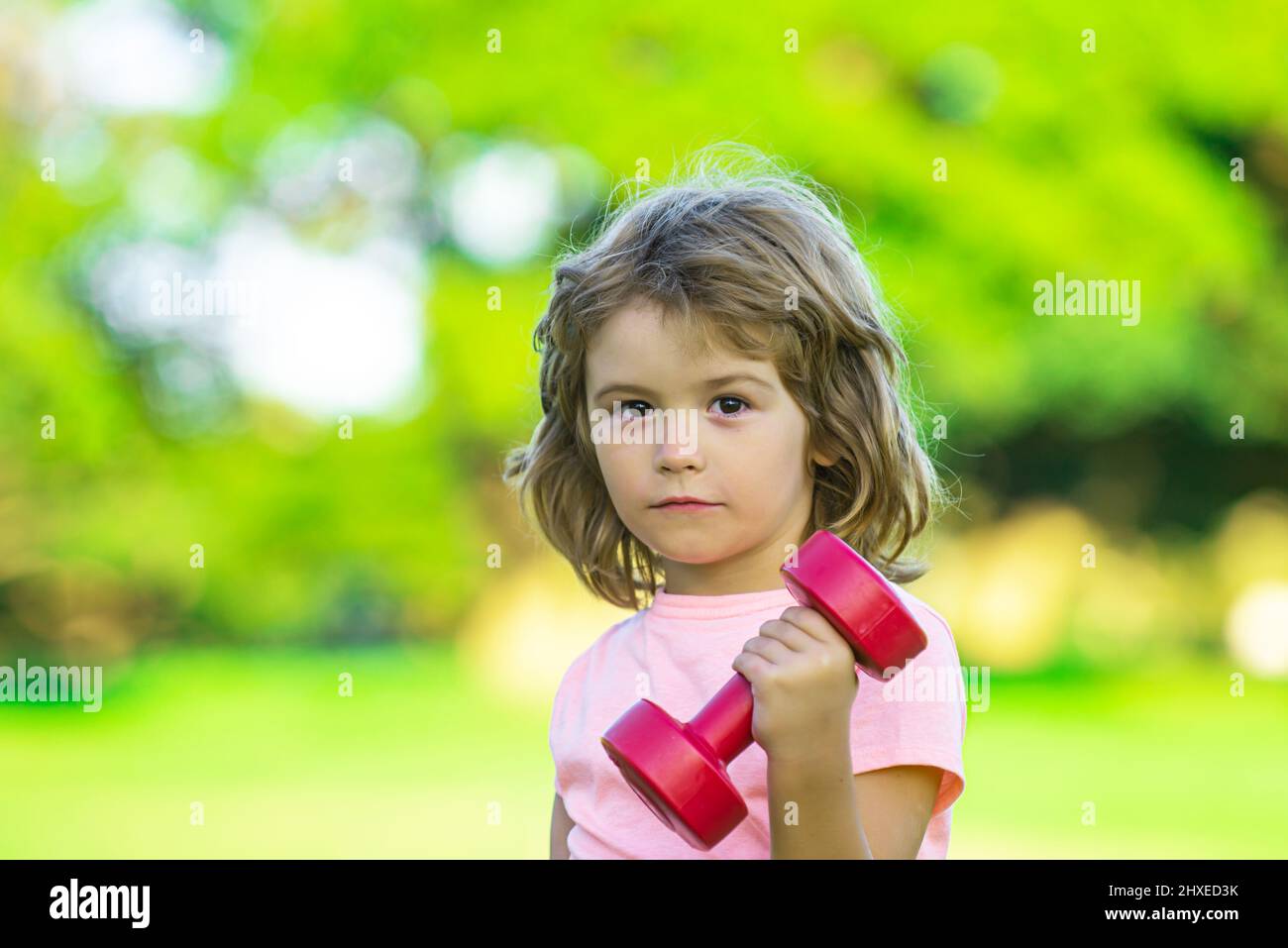 Child boy is doing exercises with dumbbells in summer park. Sport ...