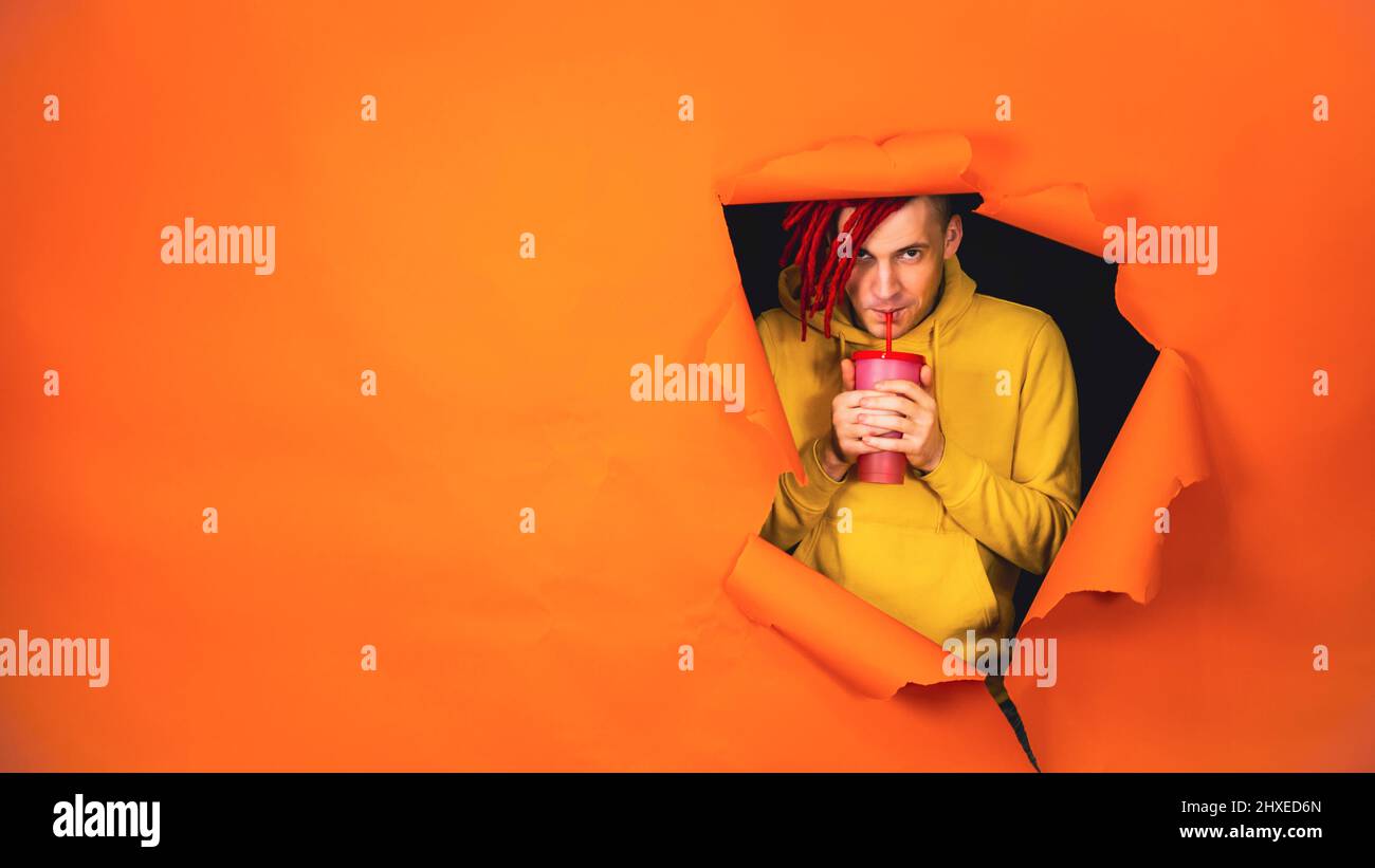 Young man drinking through soft drink straw in hole of orange ...