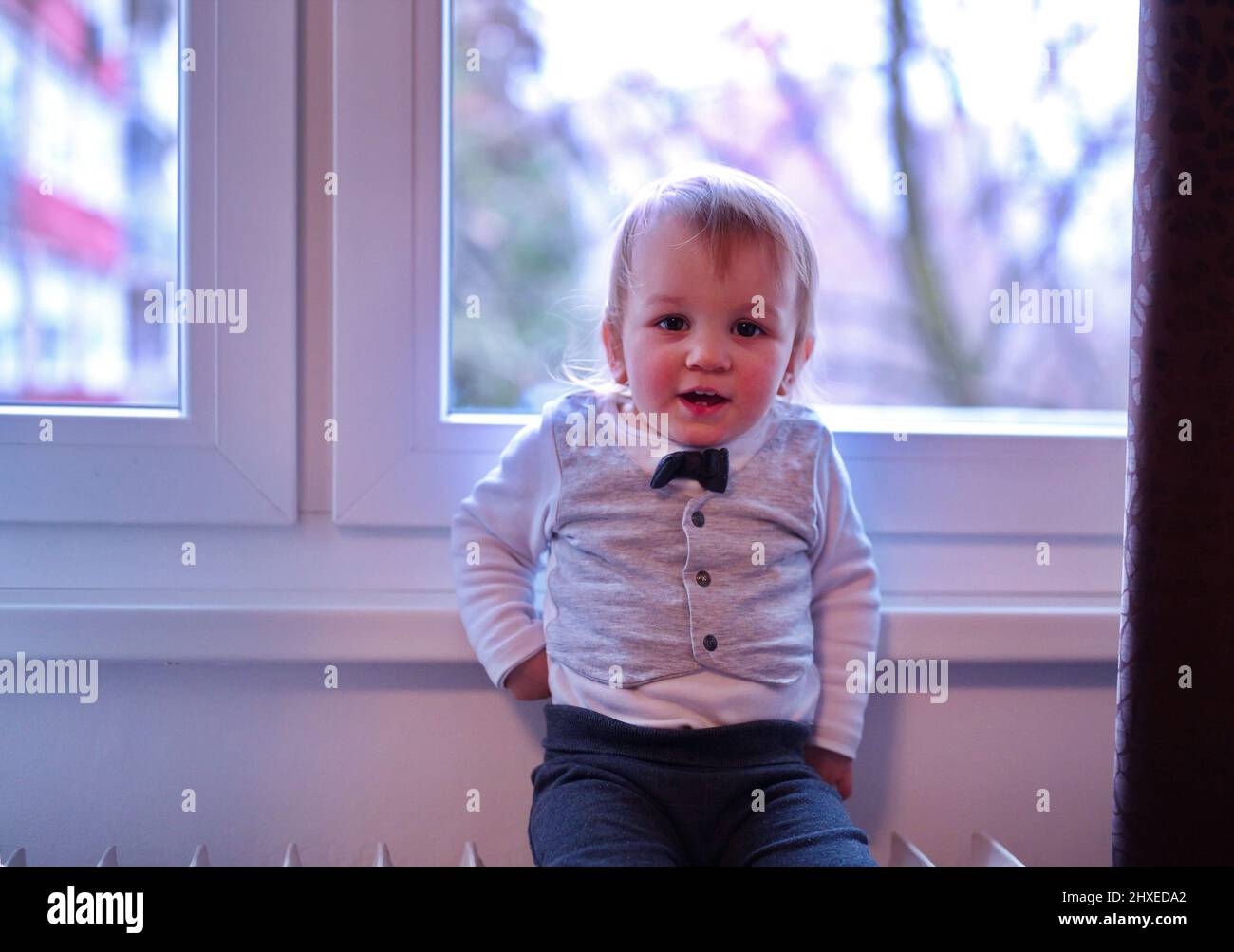 Cute little boy sitting on a radiator against the window Stock Photo ...