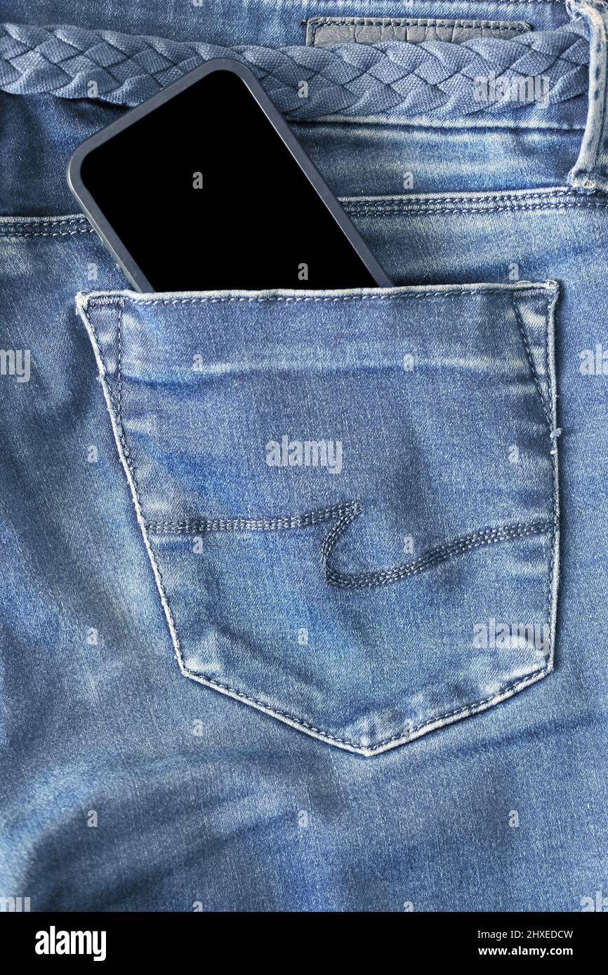 The upper part of old worn blue jeans and a smartphone with a black ...