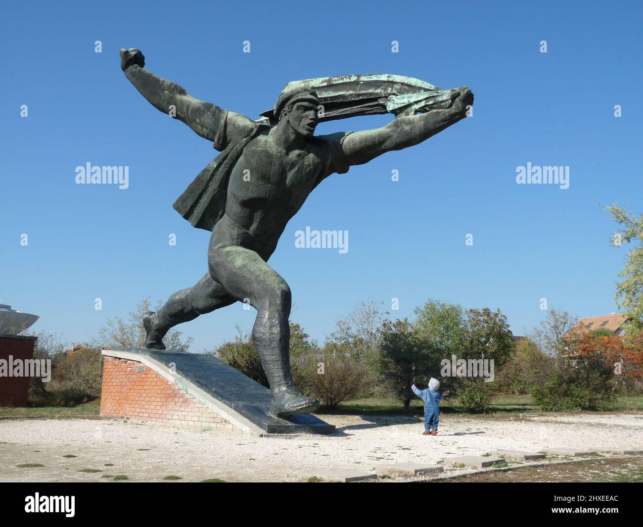 Young toddler aims a rock at a large communist statue in an open air ...