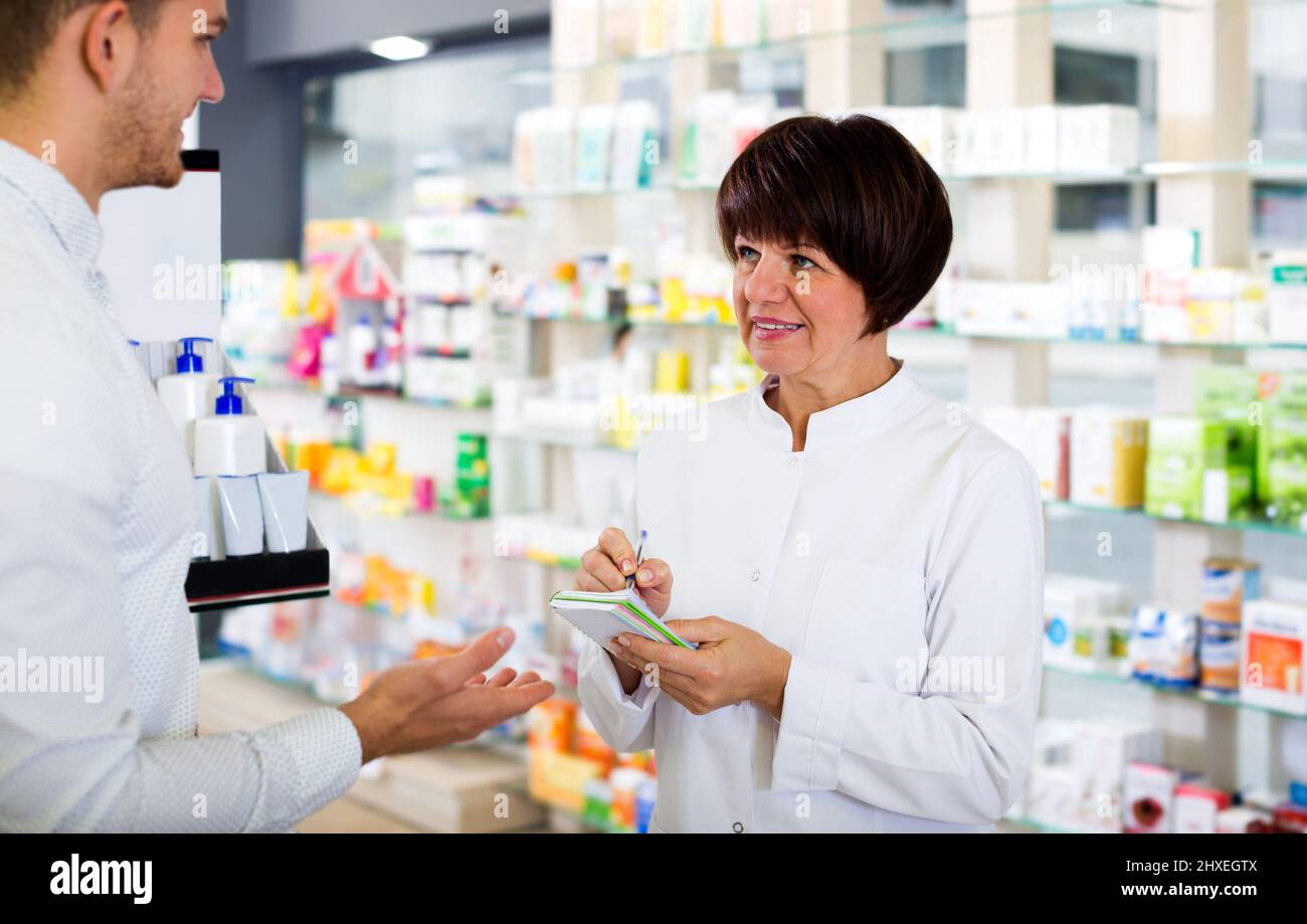 Portrait of smiling woman druggist wearing white coat giving advice to ...