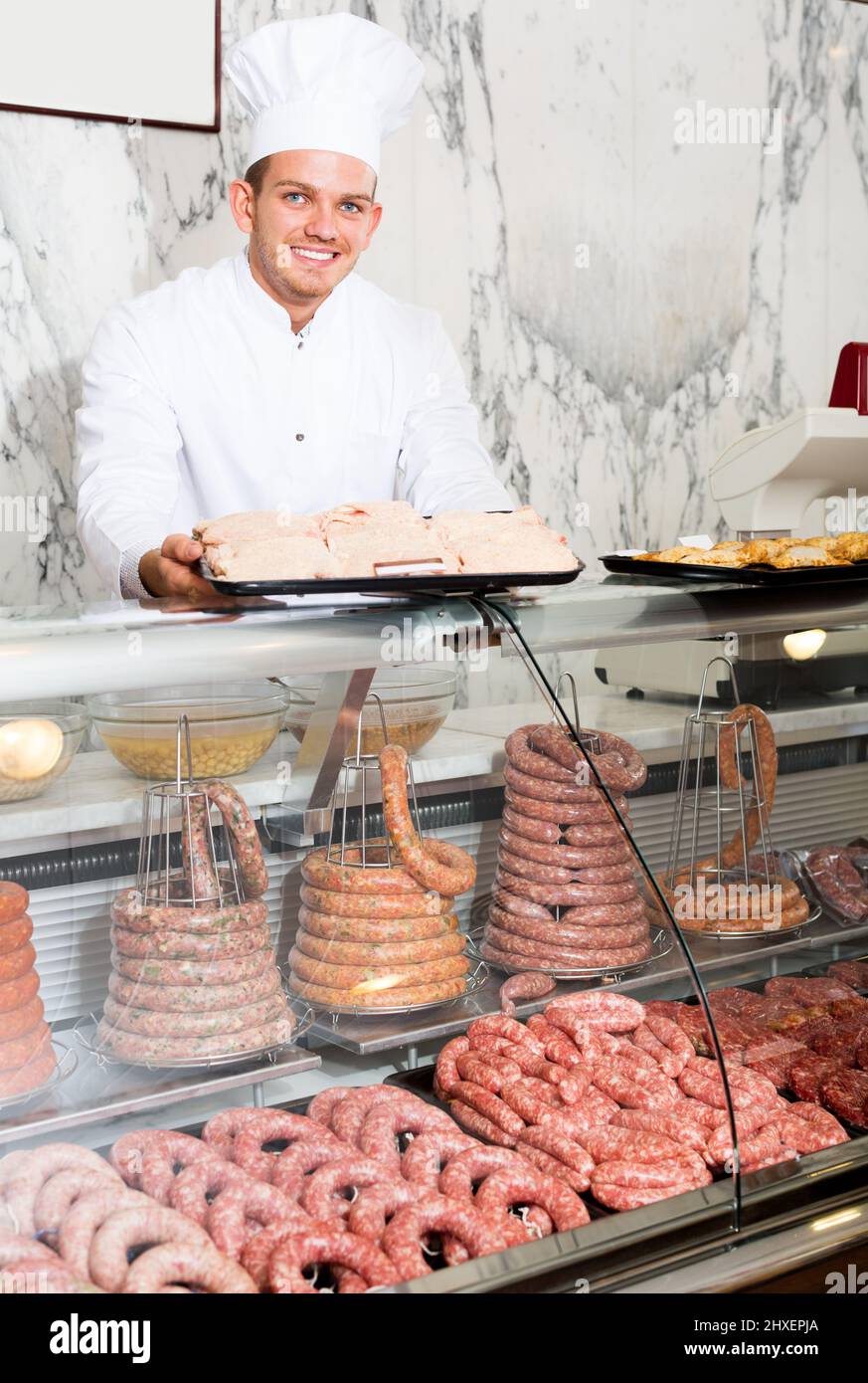 Smiling shop-boy in working clothes taking raw meat from stall Stock ...