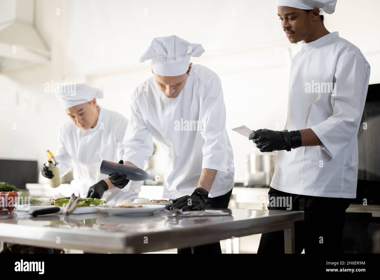 Multiracial group of cooks finishing main courses while working ...