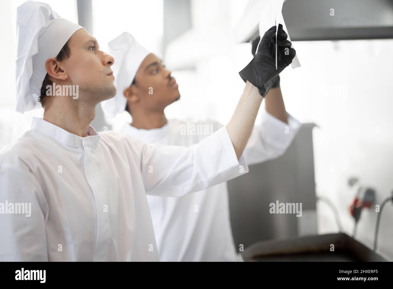 Two well-dressed chefs look on printed checks with orders while cooking ...