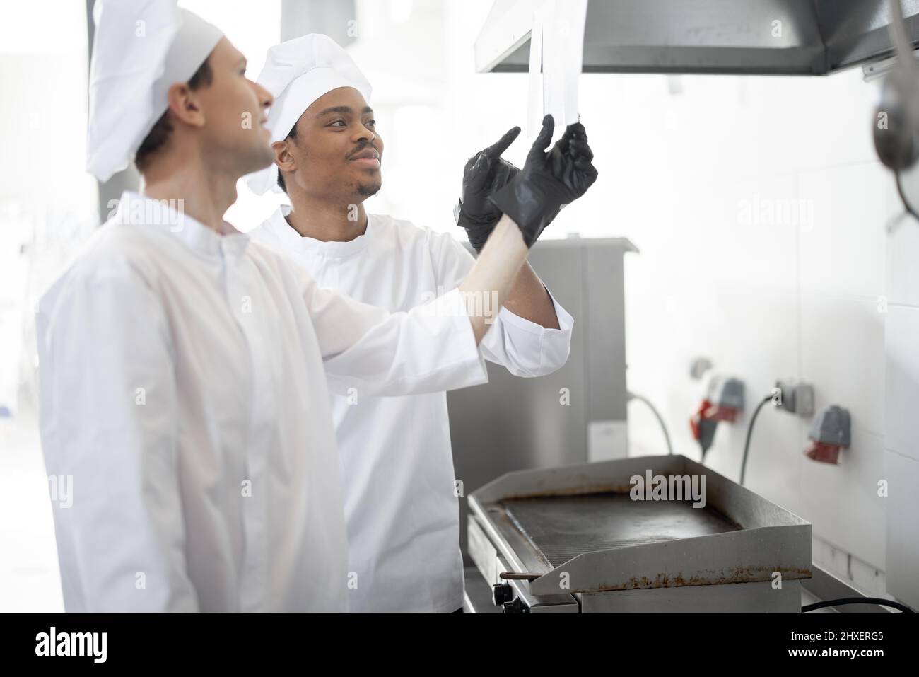 Two well-dressed chefs look on printed checks with orders while cooking ...