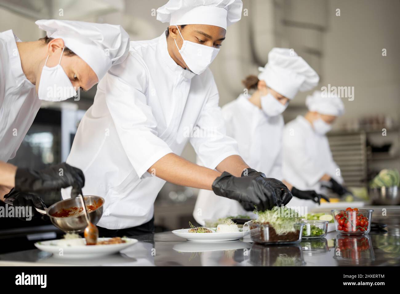Multiracial group of cooks finishing main courses while working ...