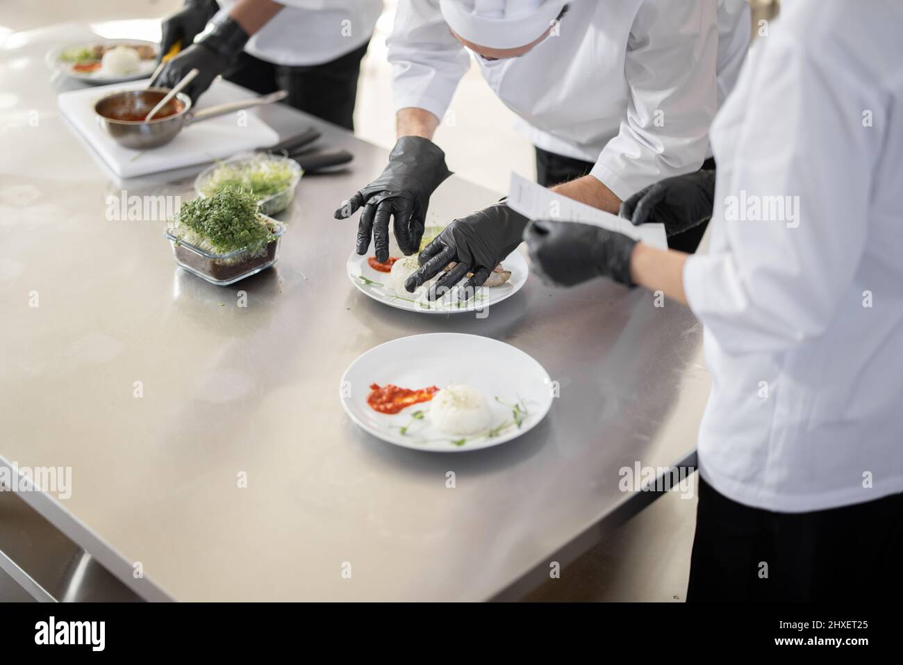 Cooks finishing main courses, putting greens on plates with rise and ...