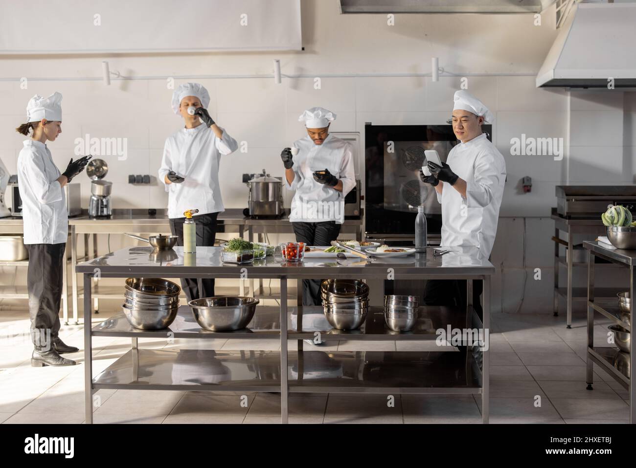 Group of cooks using phones and drinking coffee during a break in the ...