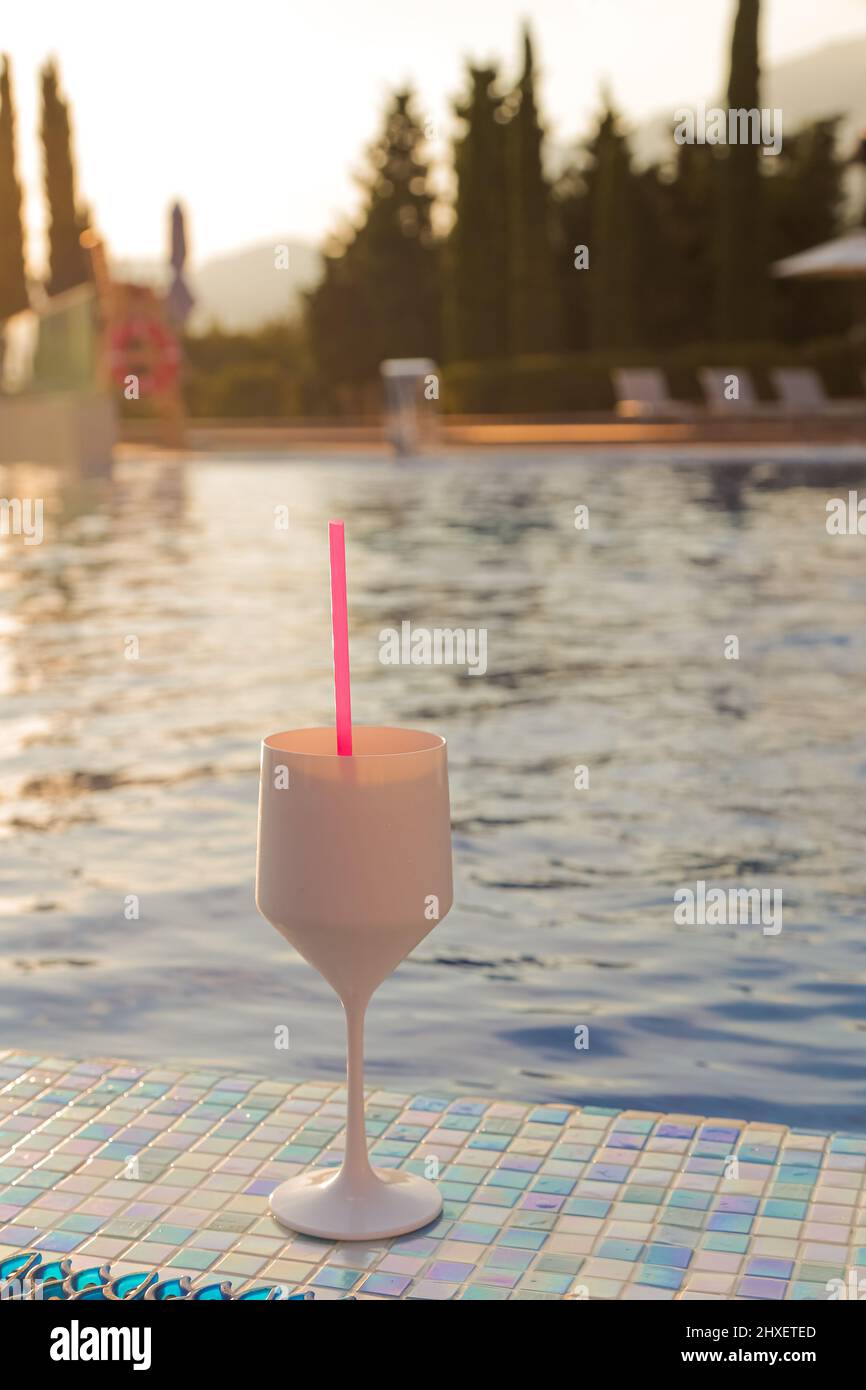 White goblet with a drink and a pink straw stands on the edge of the ...