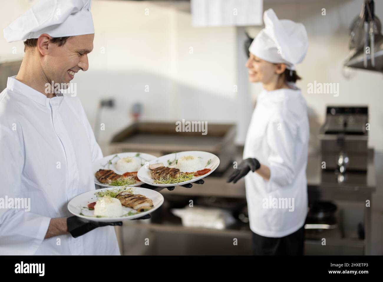 Chef standing with ready meals, talking with female cook in the kitchen ...
