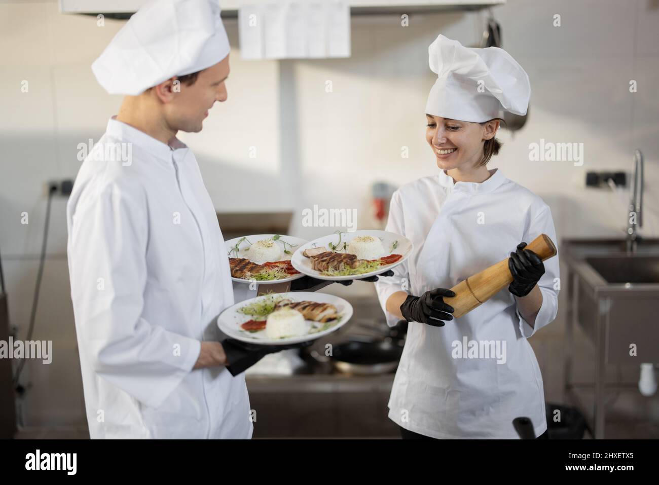 Chef standing with ready meals, talking with female cook in the kitchen ...