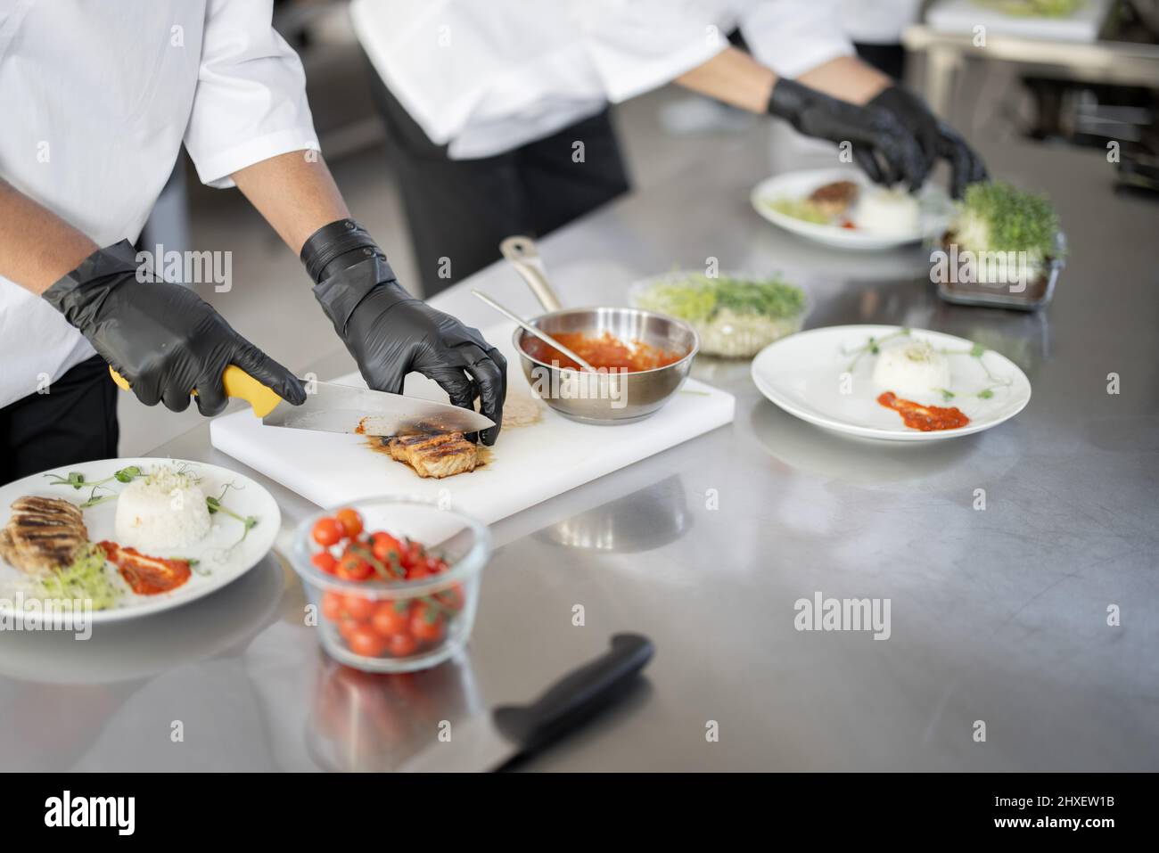 Cooks finishing main courses, putting greens on plates with rise and ...