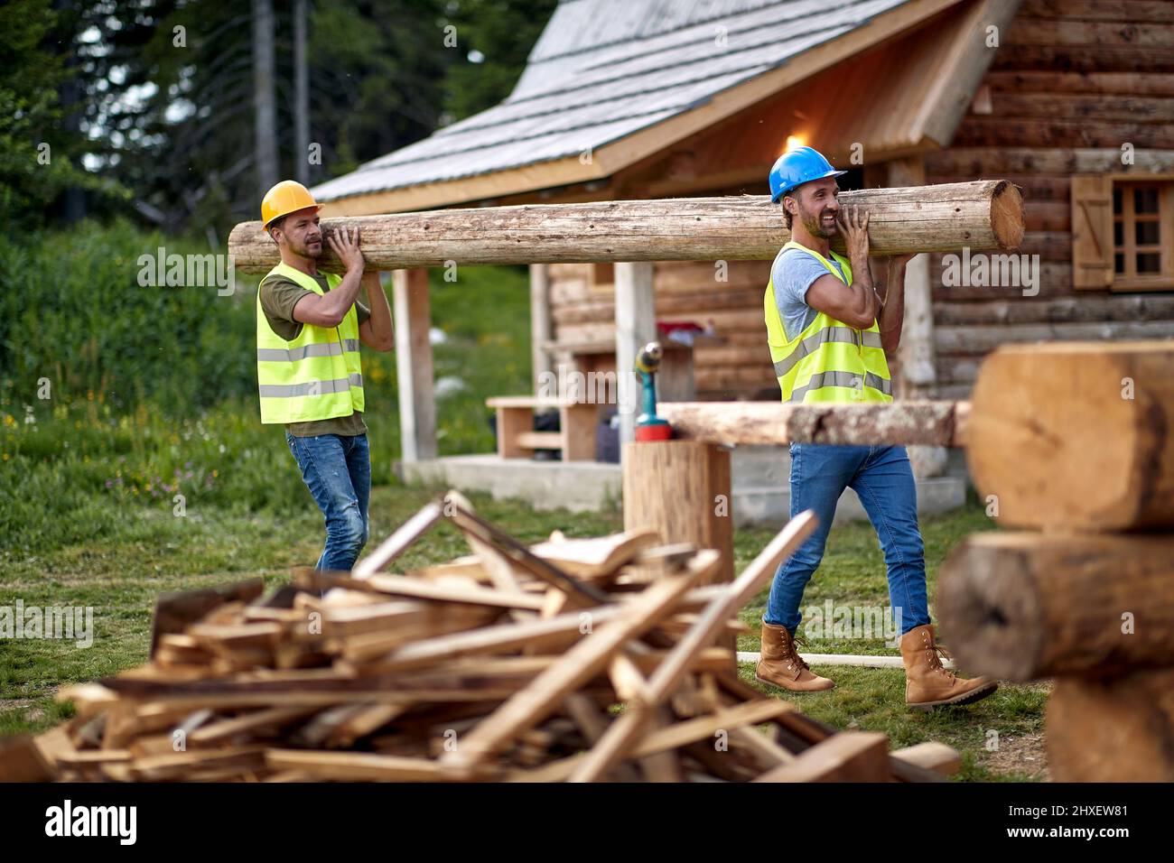 Two young male builders carry timber at cottage construction site in ...