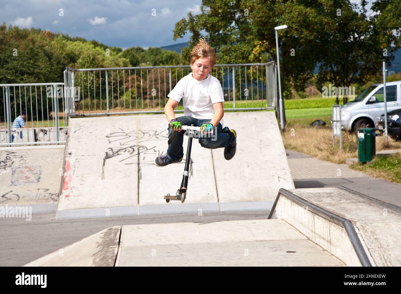 child, boy is jumping with a scooter over a fun box in the skate parc ...