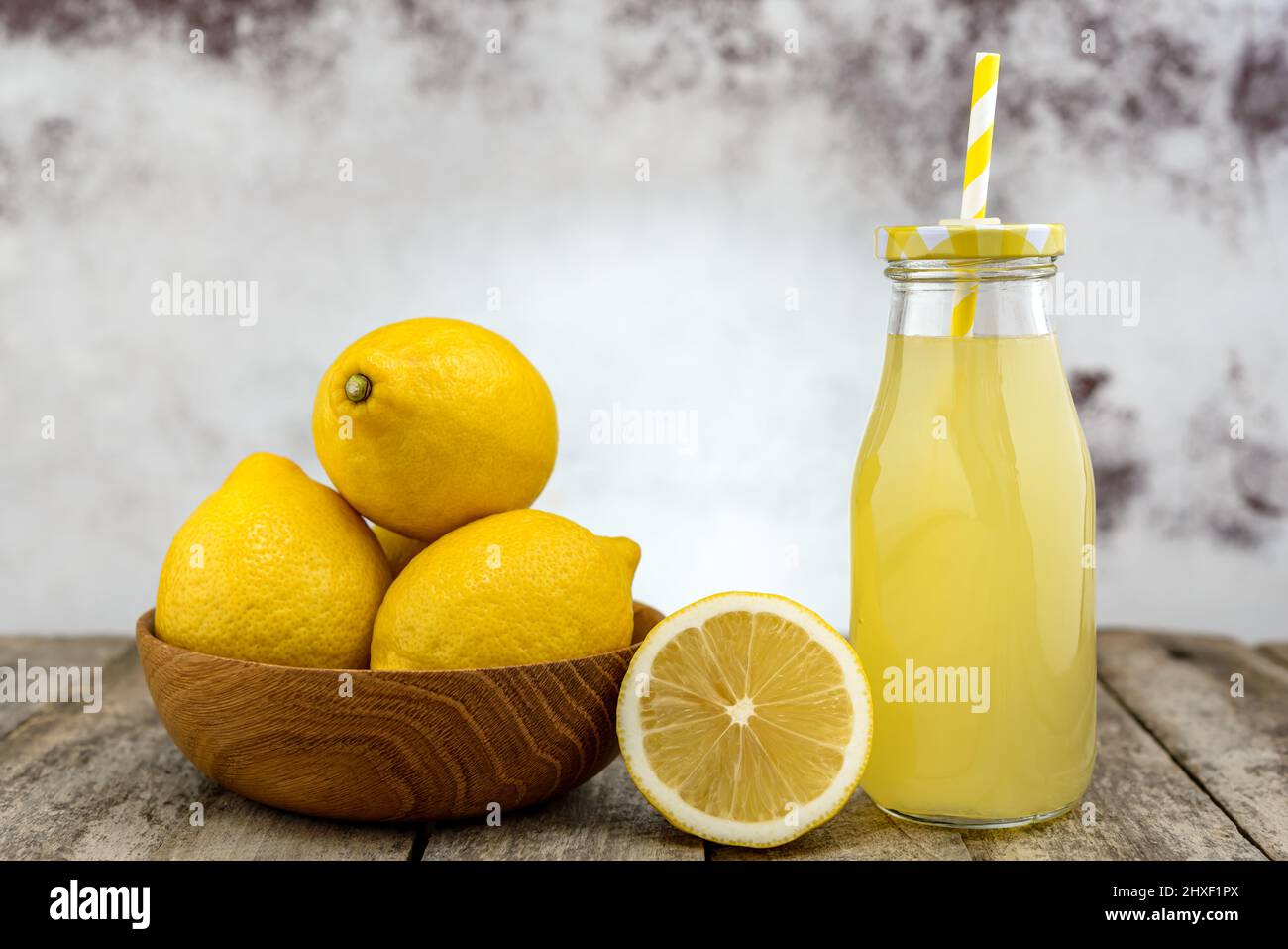 Bottle of cold lemonade with straw and wooden bowl with lemons on ...