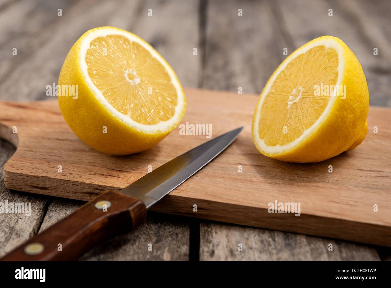 Fresh lemon cut in half with knife on wooden cutting board Stock Photo ...