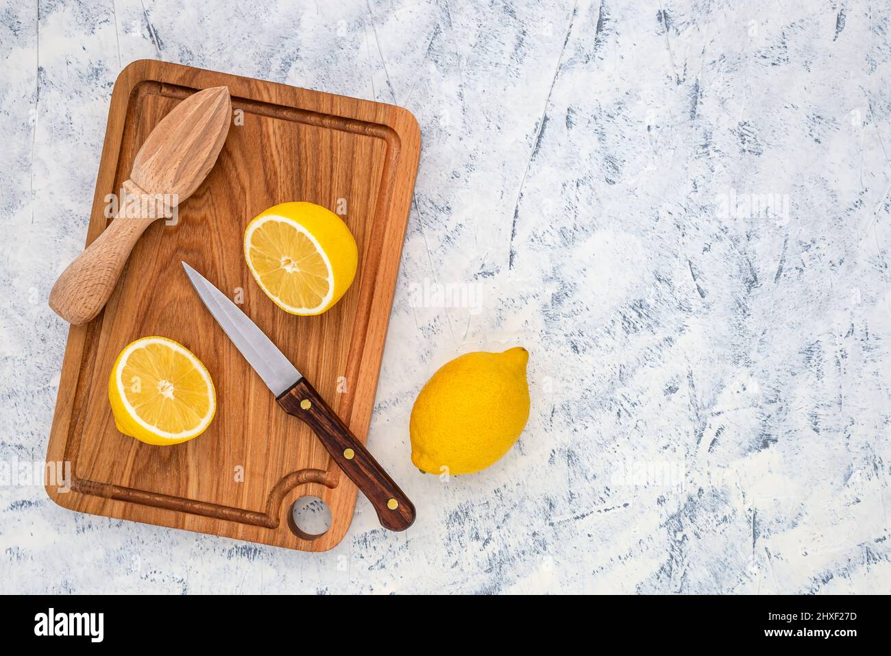 Fresh lemon cut in half with knife and juicer on wooden cutting board ...