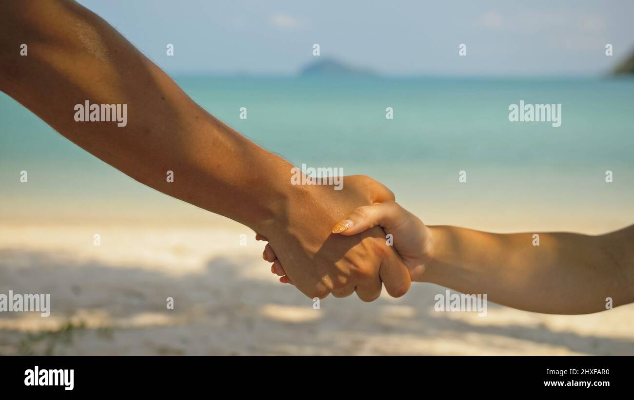 Hands of flirting young man and woman touching on beach in palms shadow ...