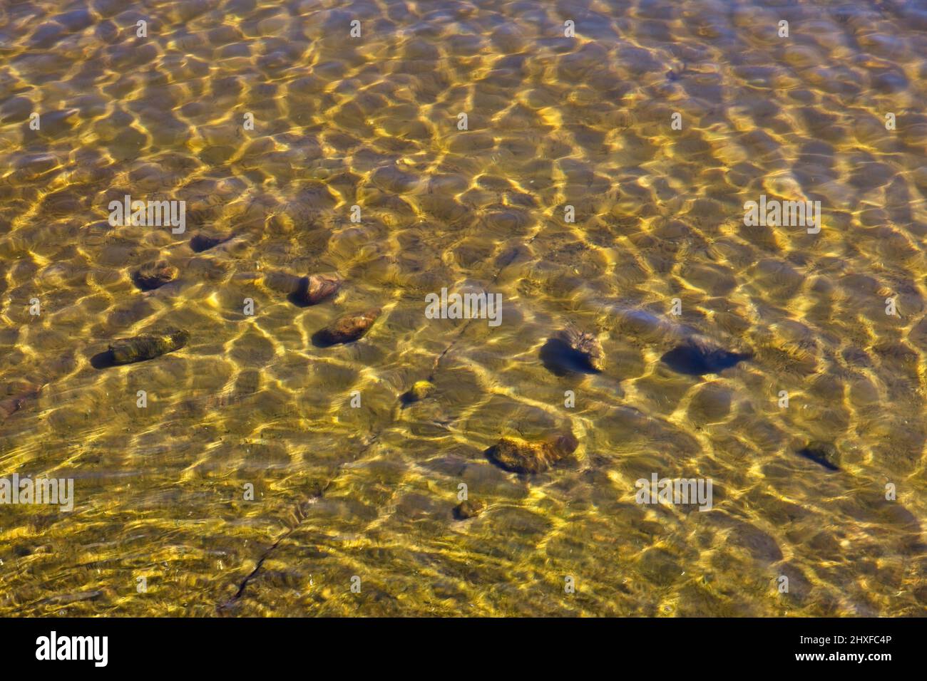 Shallow water over rock bottom with reflections and small rippling ...