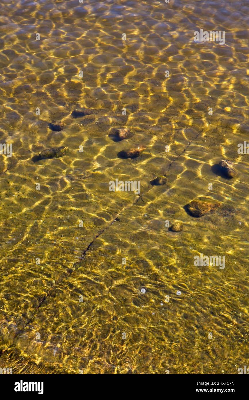 Shallow water over rock bottom with reflections and small rippling ...