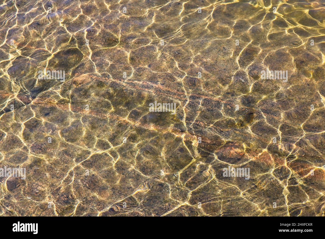 Shallow water over rock bottom with reflections and small rippling ...