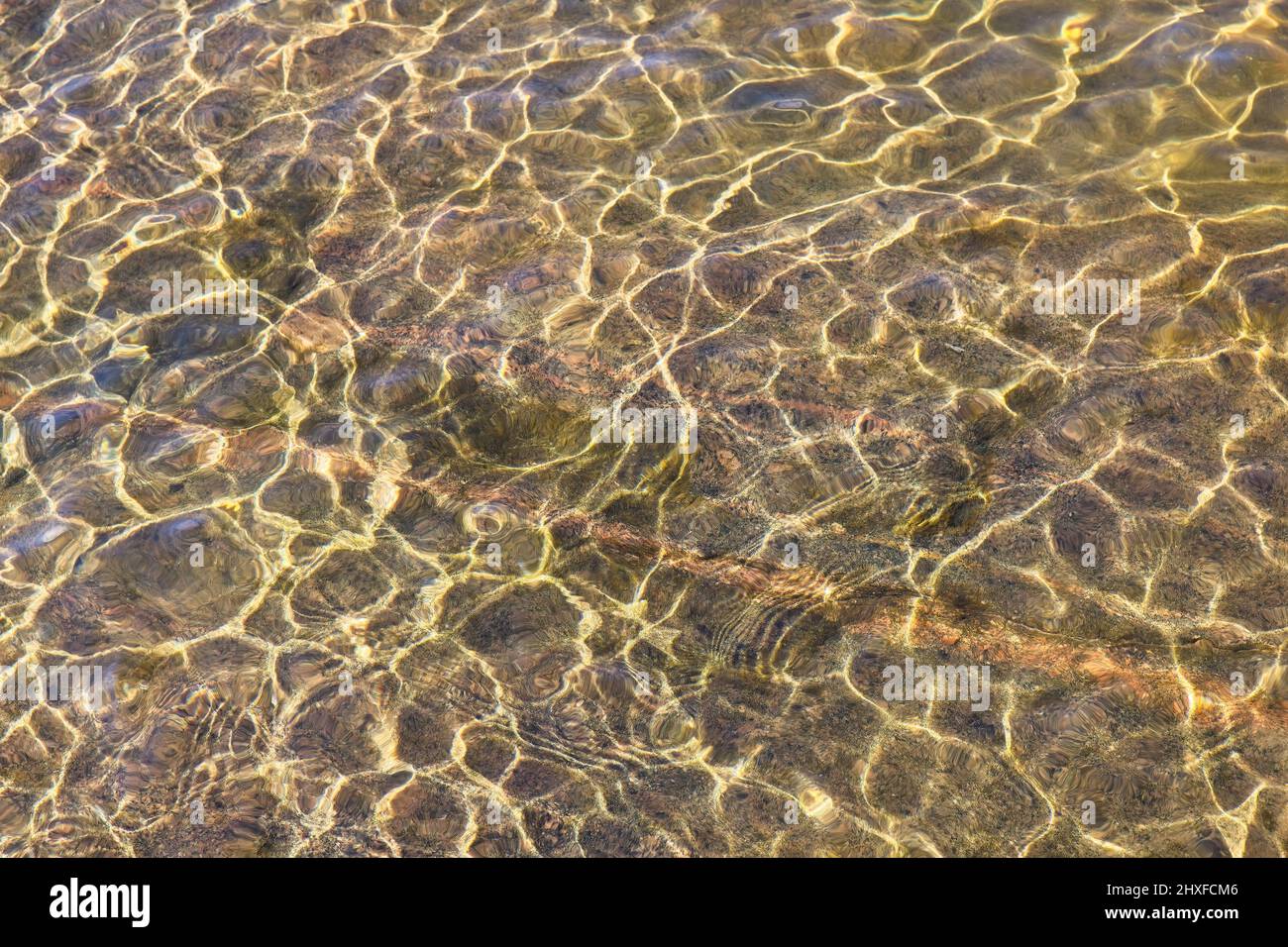 Shallow water over rock bottom with reflections and small rippling ...