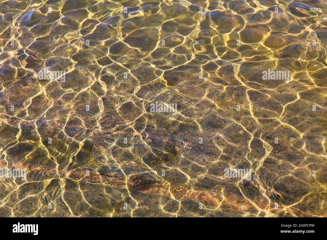 Shallow water over rock bottom with reflections and small rippling ...