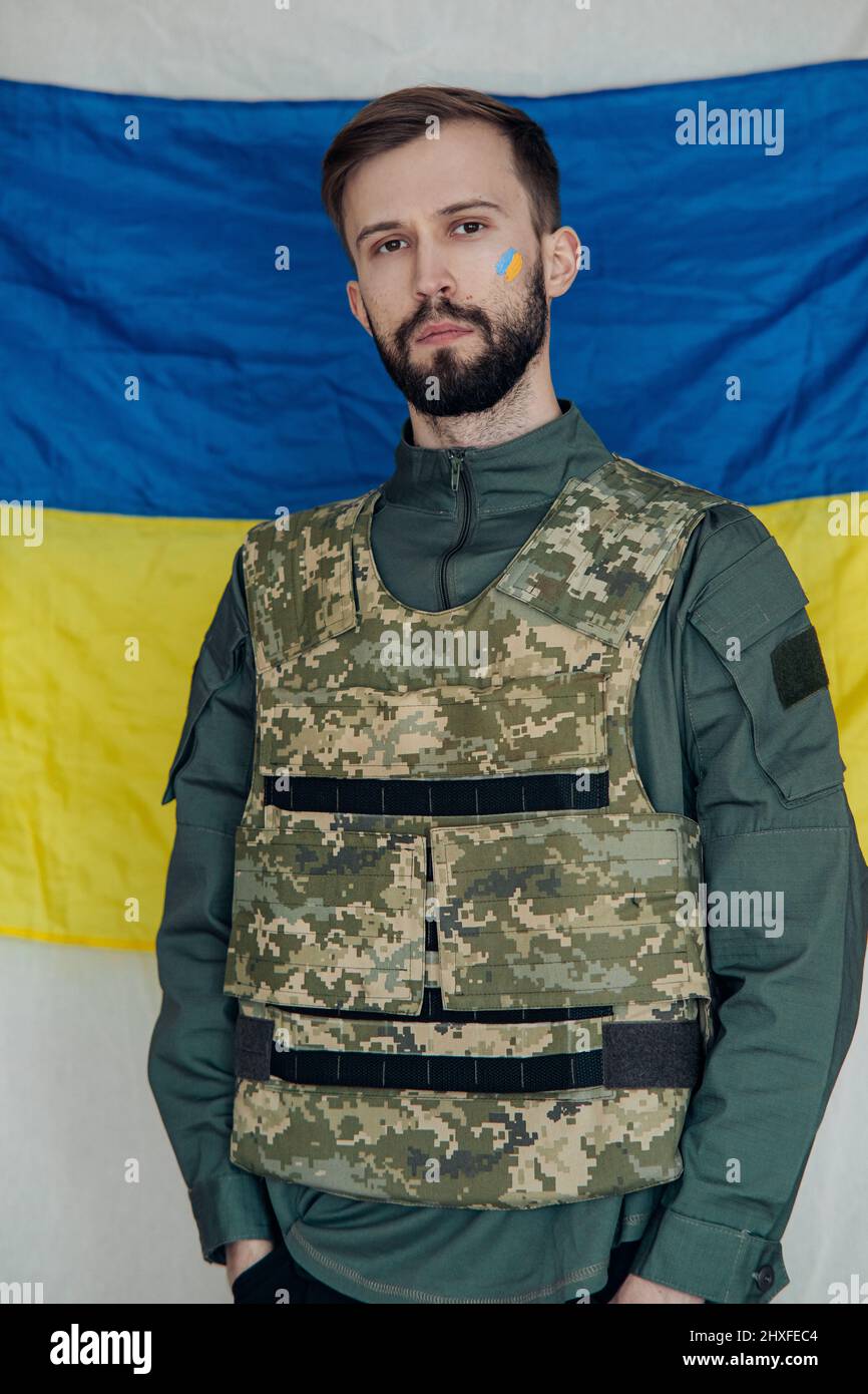 Portrait of young angry man in body armor with ukrainian flag on his ...
