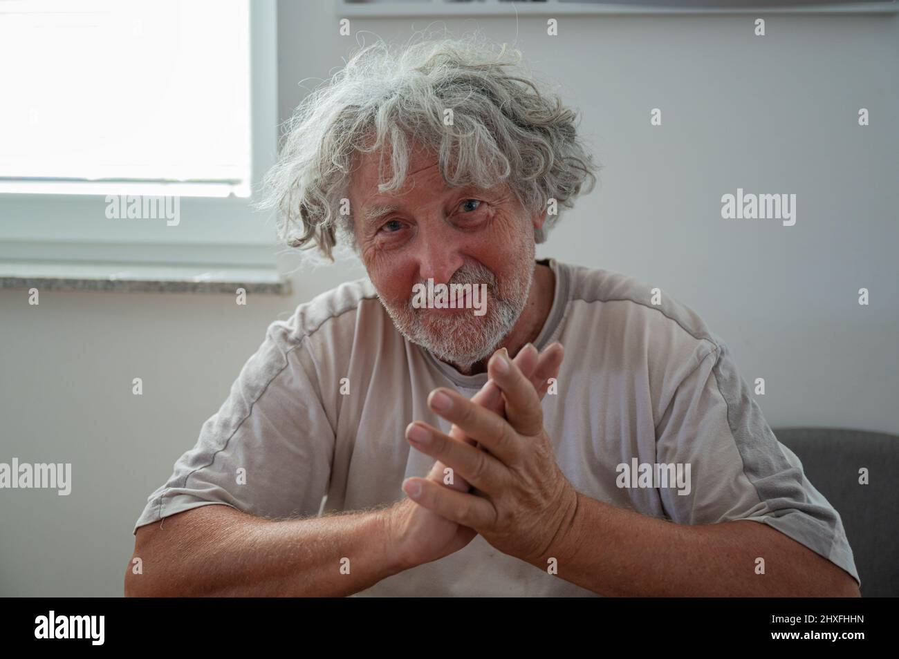 Portrait of a senior man with wrinkles and grey curly hair sitting at ...