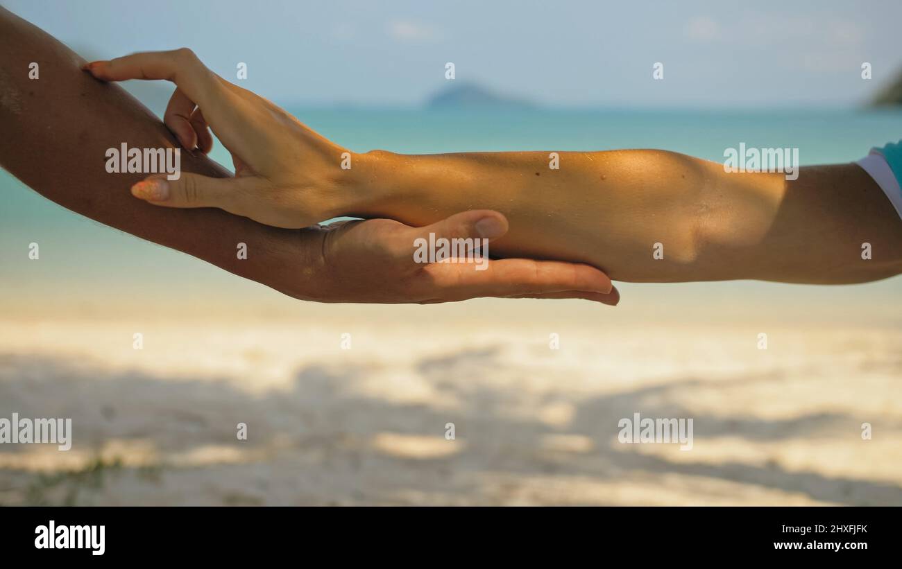 Hands of flirting young man and woman touching on beach in palms shadow ...