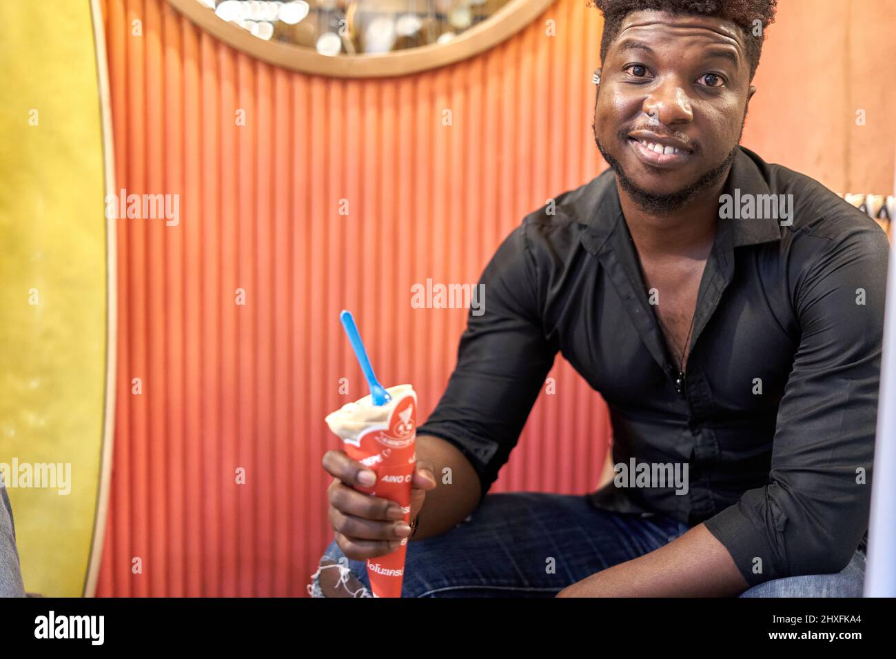 Portrait of an african man eating ice cream while sitting on a mall ...