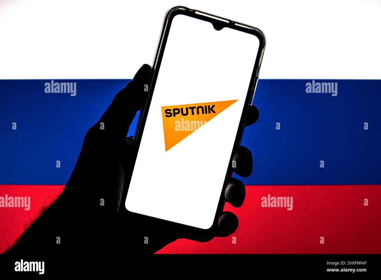 In this photo illustration a Sputnik logo seen displayed on a smartphone with a flag of Russia ...