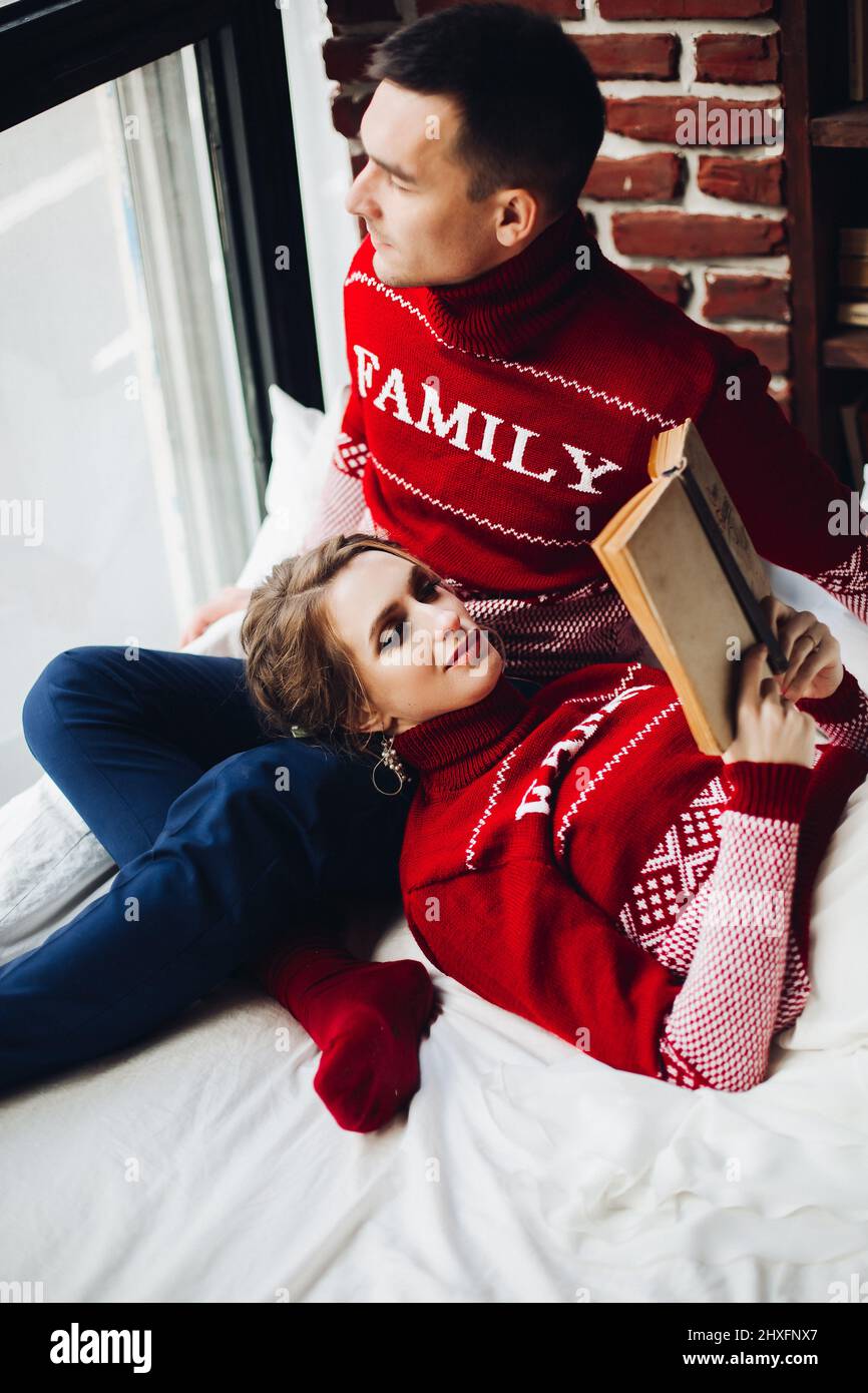 Couple in red sweaters relaxing in bed, reading together Stock Photo ...
