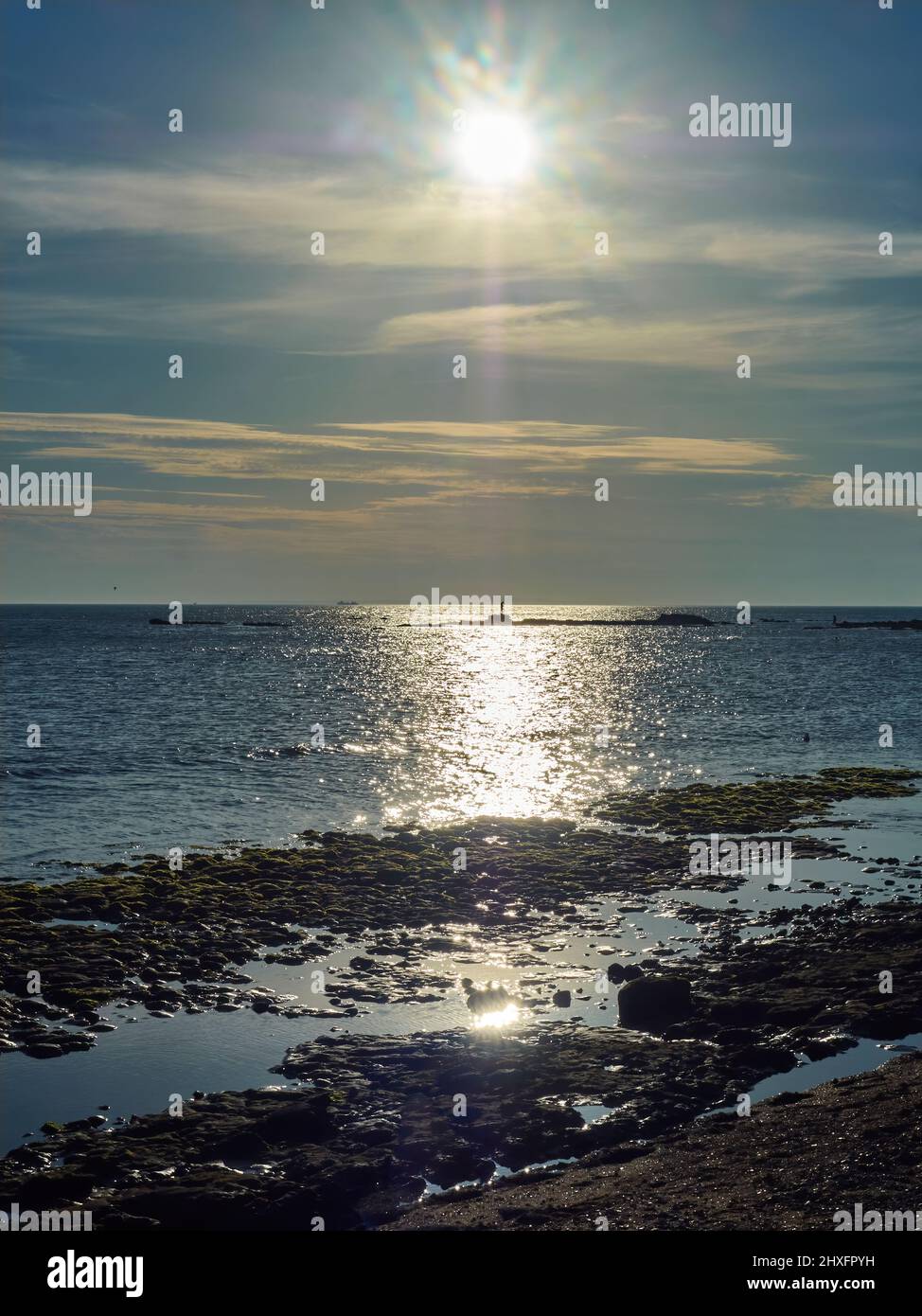 A setting sun with beams reflected into a golden pathway reaching from ...