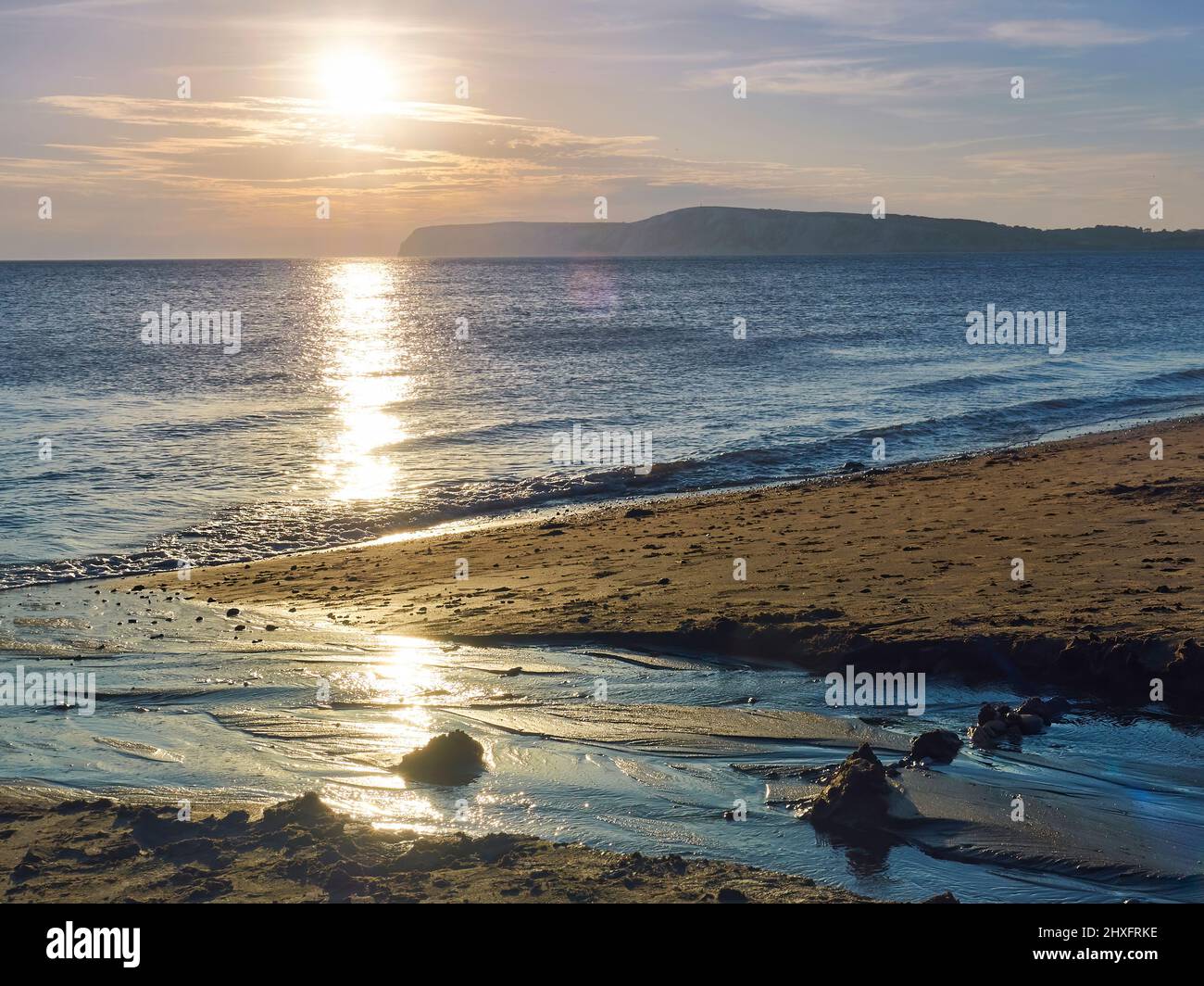A descending sun, heading towards silhouetted headland, throws a ...