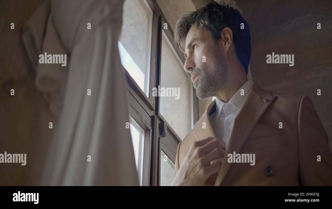 Man in suit is standing by window. Action. Elegant man in light suit is ...