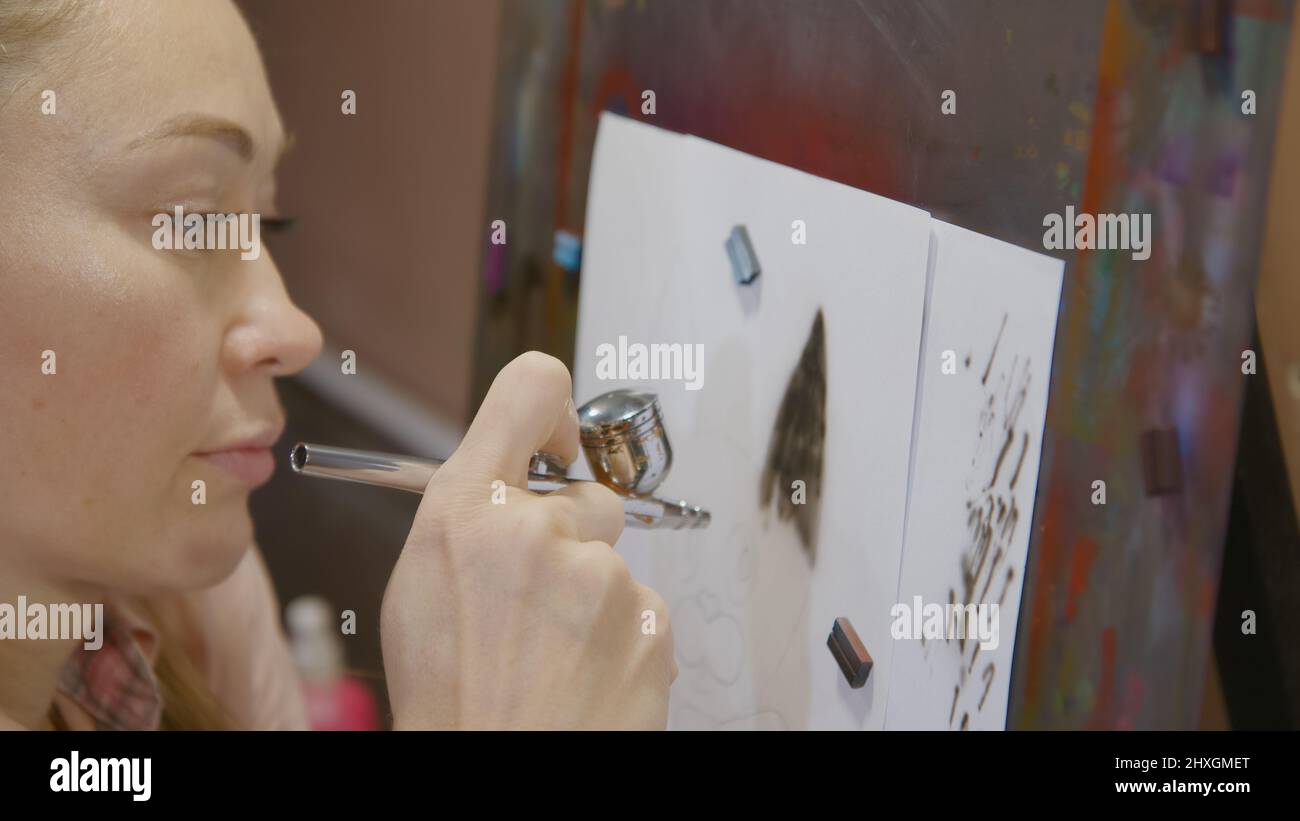 Woman artist learns to paint with airbrush with acrylic dye, paper and ...