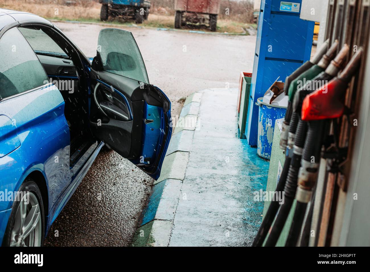 Blue car parked at gas, petrol station for fuel refill. Rainy, cold ...