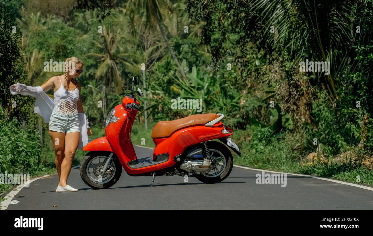 Woman on red scooter in white clothes drive on forest road trail ...