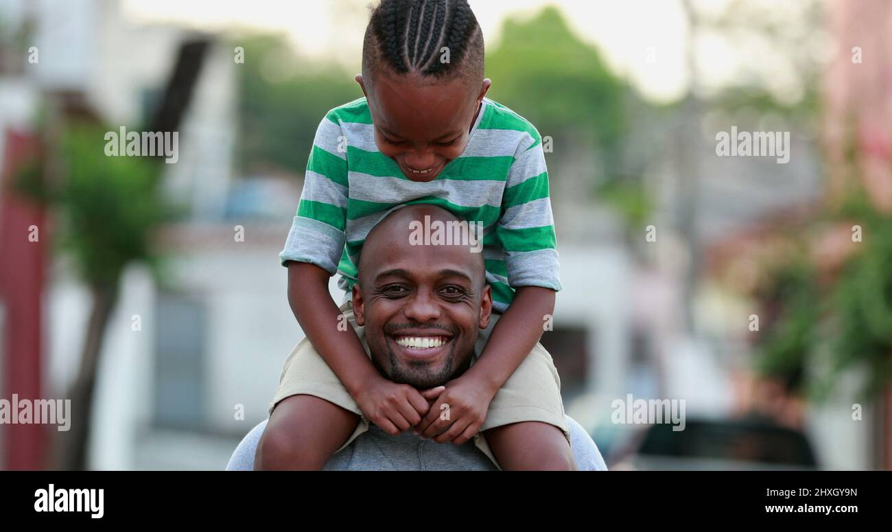 Son on top of father shoulders outside. African black parent and child ...