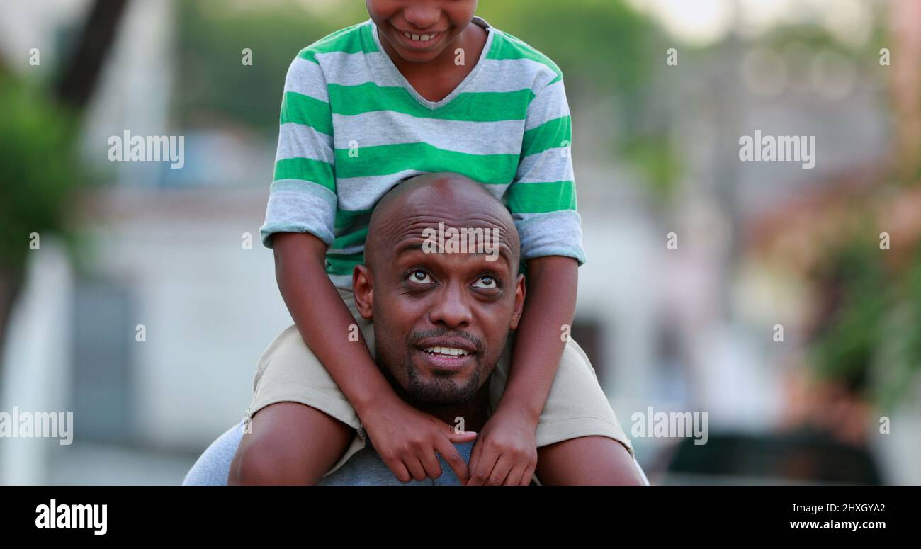 Son on top of father shoulders outside. African black parent and child ...