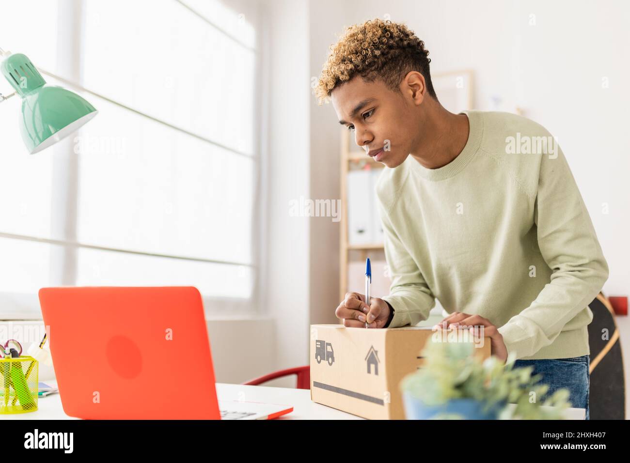 Young adult man copying costumer address from email on package before ...